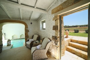 Quarto com paredes de pedra, piscina, móveis de vime e vista para o campo.