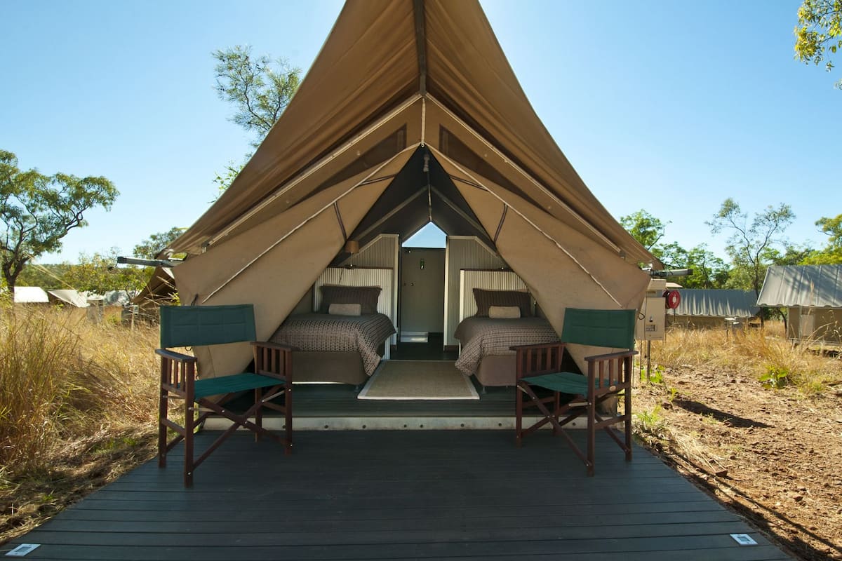 Acomodação em tenda com dois quartos, cada um contendo uma cama e uma cadeira, e entrada central.