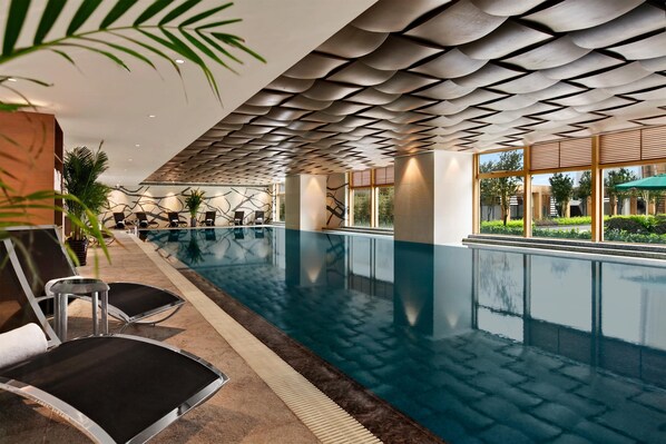 Uma piscina interior com design moderno, incluindo um padrão de teto único e amplas janelas com vista para o exterior.