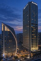 Um hotel moderno com fachada curva e um edifício alto adjacente com janelas iluminadas.