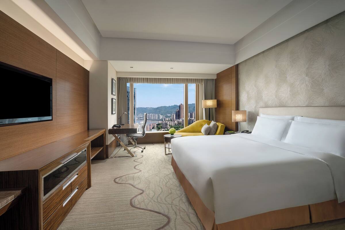 Quarto de hotel com uma cama grande, televisão, escrivaninha e vista da cidade.