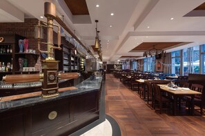 Um restaurante com um balcão comprido, mesas de madeira e uma parede de tijolos.