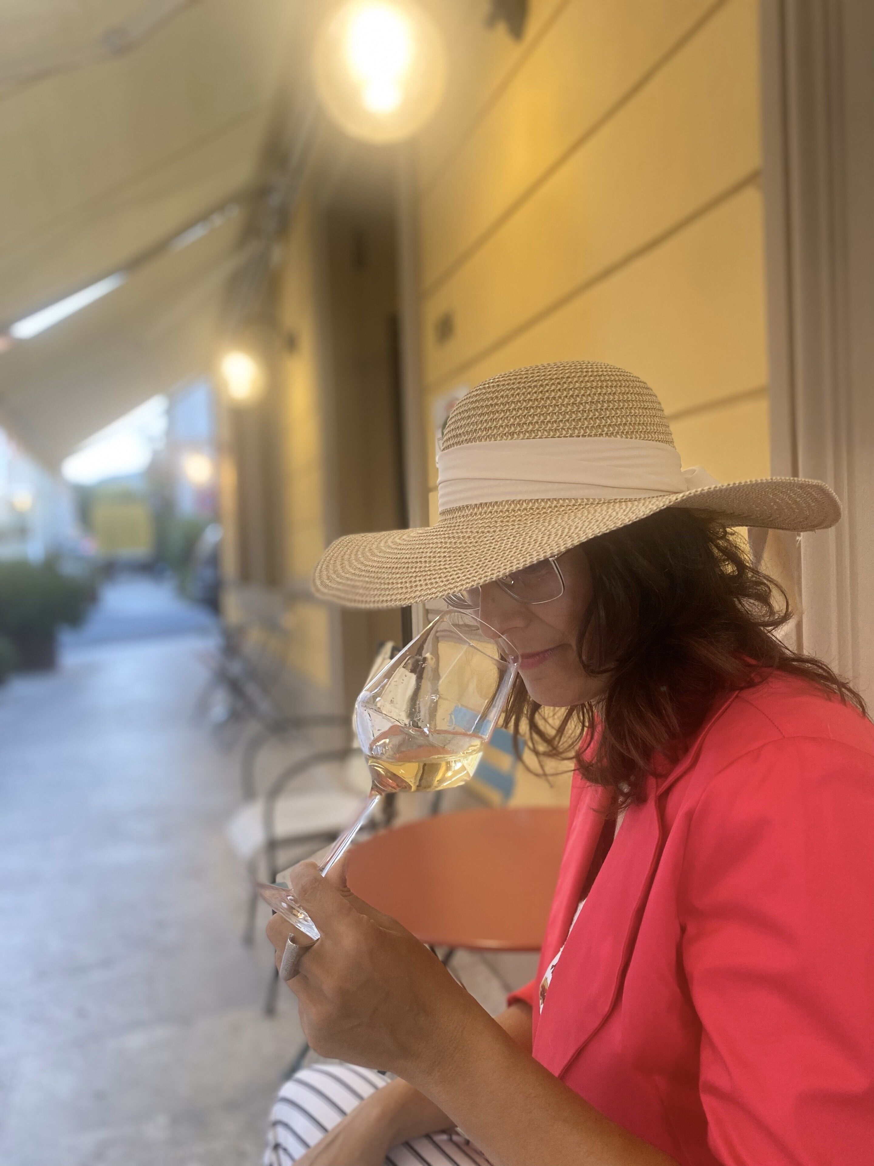 Uma pessoa sentada num café ao ar livre, segurando uma taça de vinho.