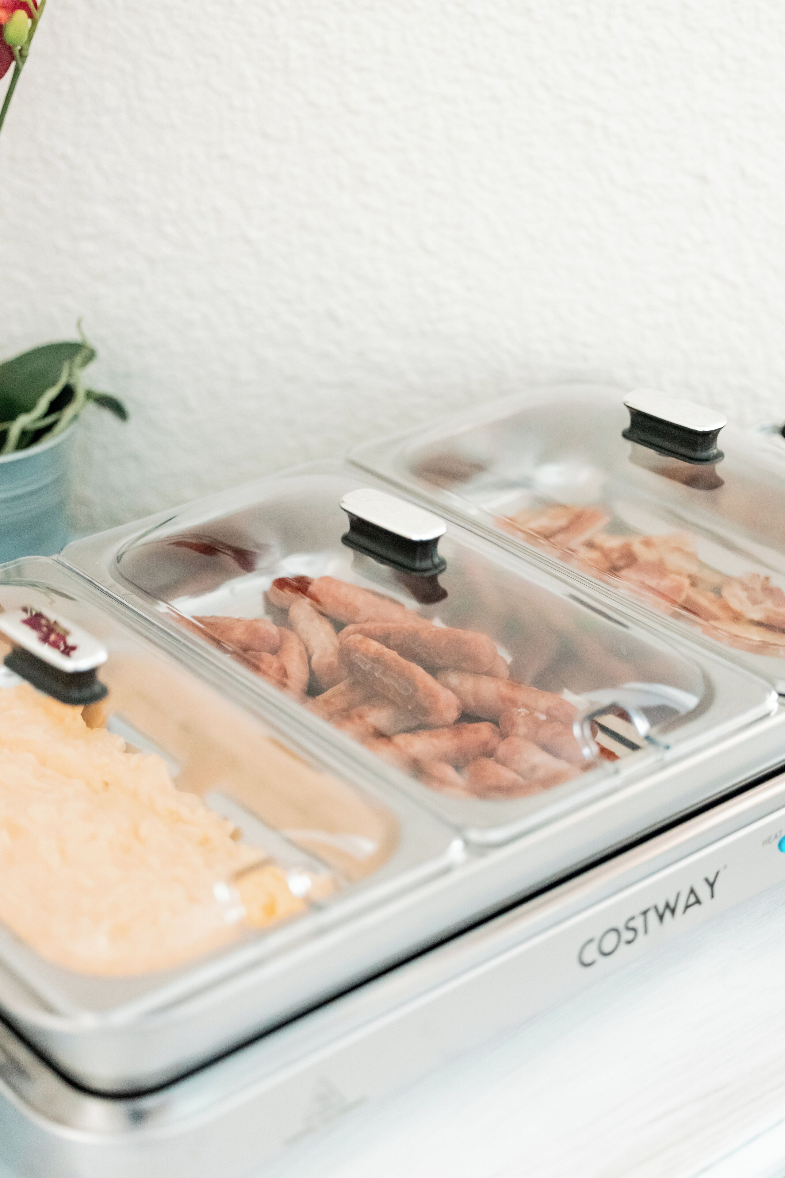 Disposição de buffet com diversos alimentos em recipientes transparentes, identificados com a marca "COSTWAY".