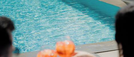 Piscina com espreguiçadeiras e uma mesa com bebidas.