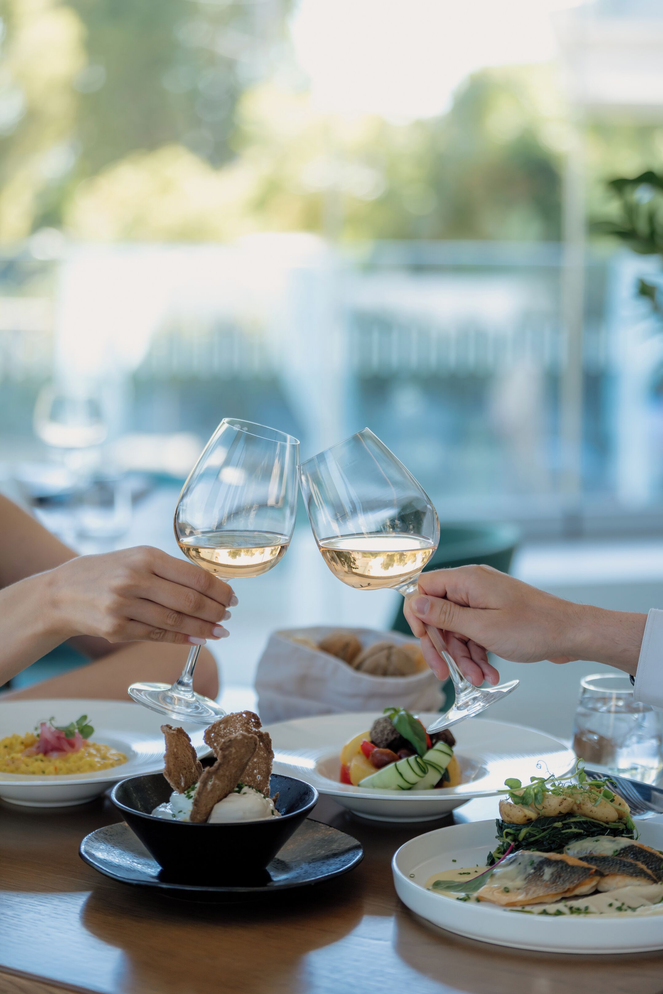 Uma mesa de jantar com vários pratos e duas pessoas brindando com taças de vinho.