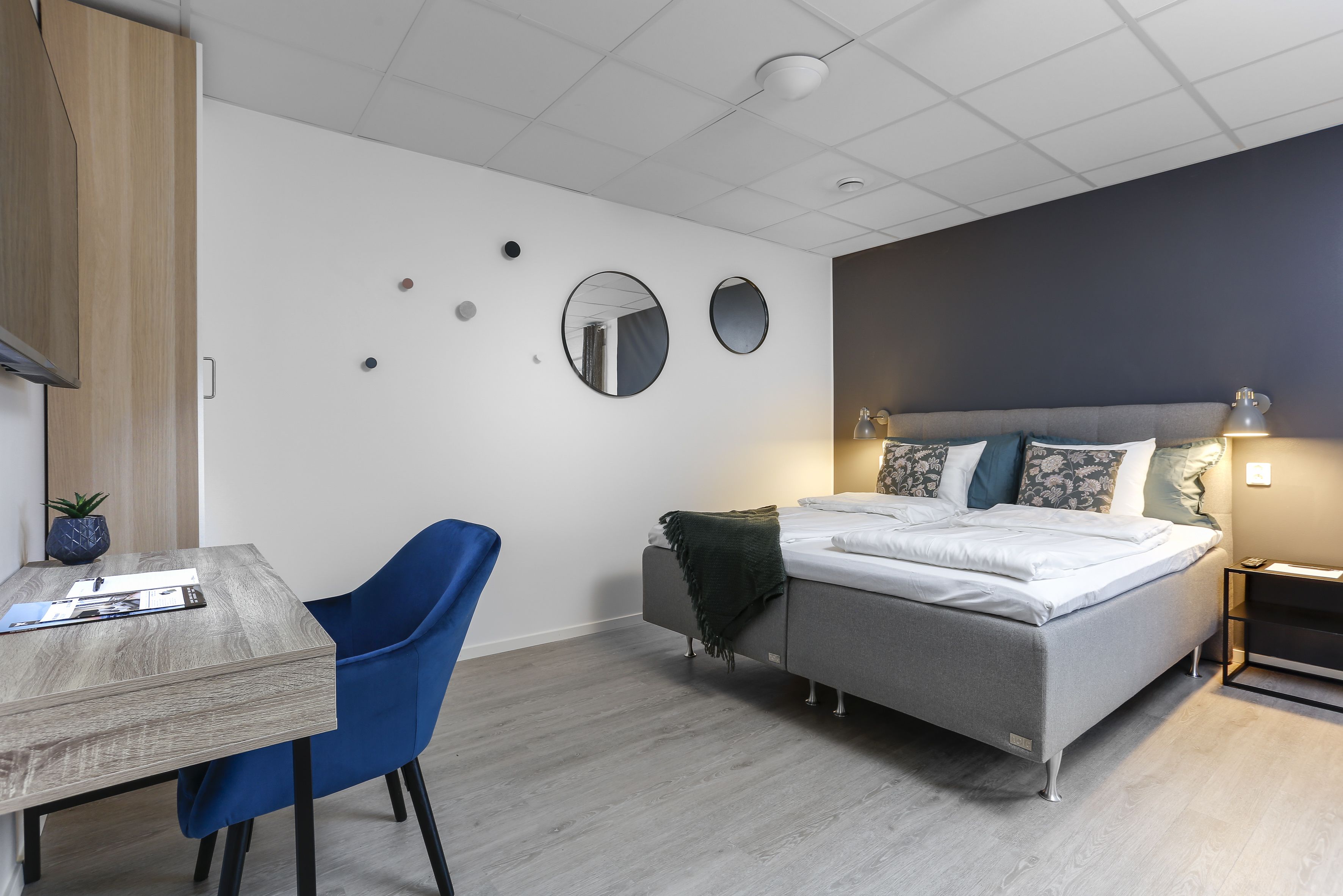 Quarto moderno com cama, mesa de cabeceira, luminária e escrivaninha com cadeira.
