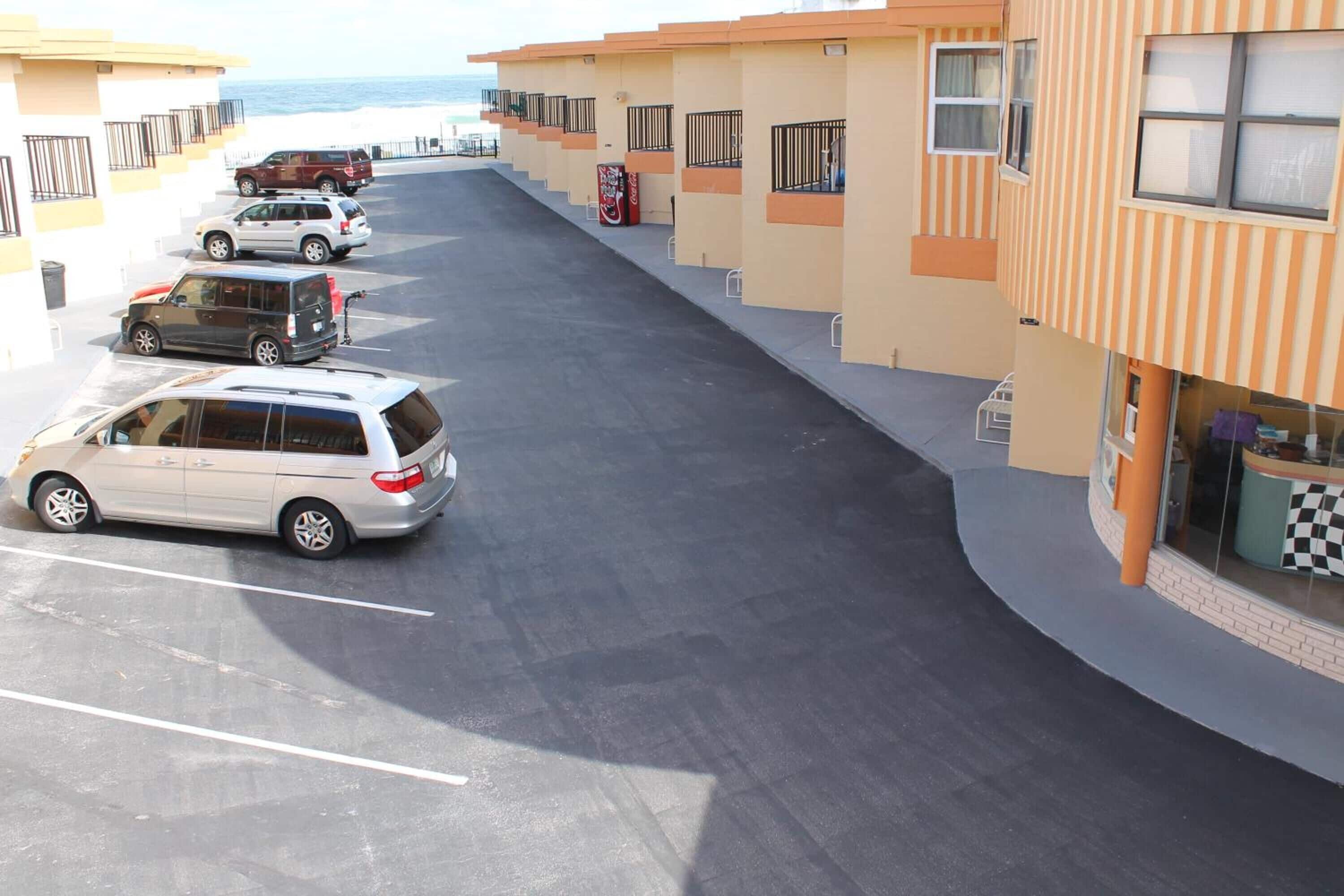 Um estacionamento com vários carros, um edifício de paredes laranja e bege, e vista para o oceano.