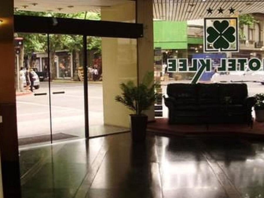 Entrada de hotel com porta de vidro, balcão de recepção e placa com o nome do hotel.