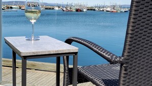 Mesa com copo de vinho branco e cadeira de vime à beira-mar.