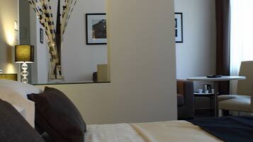 Quarto de hotel com uma cama, uma escrivaninha, uma cadeira, um abajur e um espelho.