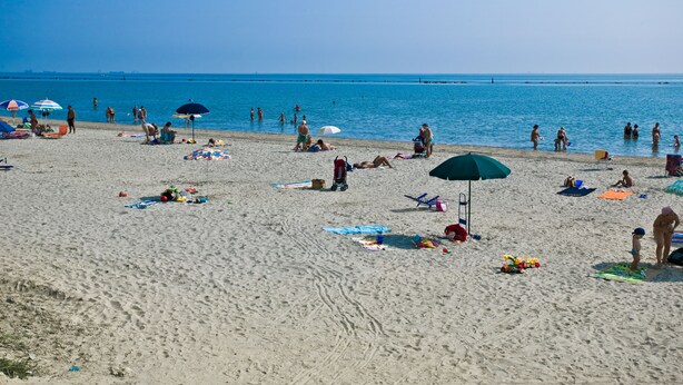 Uma praia com pessoas tomando sol, guarda-sóis e cadeiras de praia.