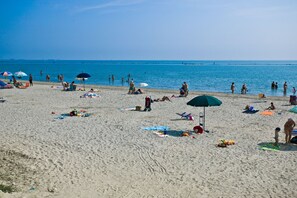 Uma praia com pessoas tomando sol, guarda-sóis e cadeiras de praia.