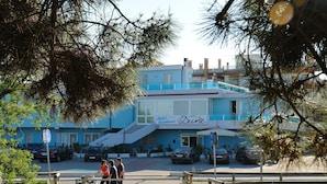 Um hotel chamado "Hotel Residence Le Dune" com design moderno, apresentando um esquema de cores azul e branco, uma escadaria que leva à entrada e uma área de estacionamento com vários carros.