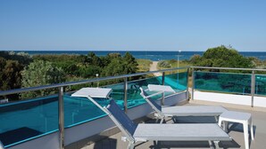 Piscina no terraço com bordas de vidro transparente, espreguiçadeiras e vista para o mar.