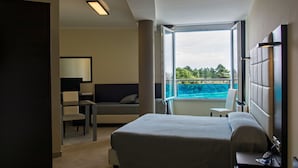 Quarto de hotel moderno com uma cama grande, uma escrivaninha, uma cadeira e varanda com vista para o mar.