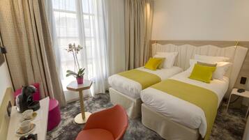 Quarto de hotel com duas camas, uma mesinha com planta em vaso, máquina de café e uma cadeira.