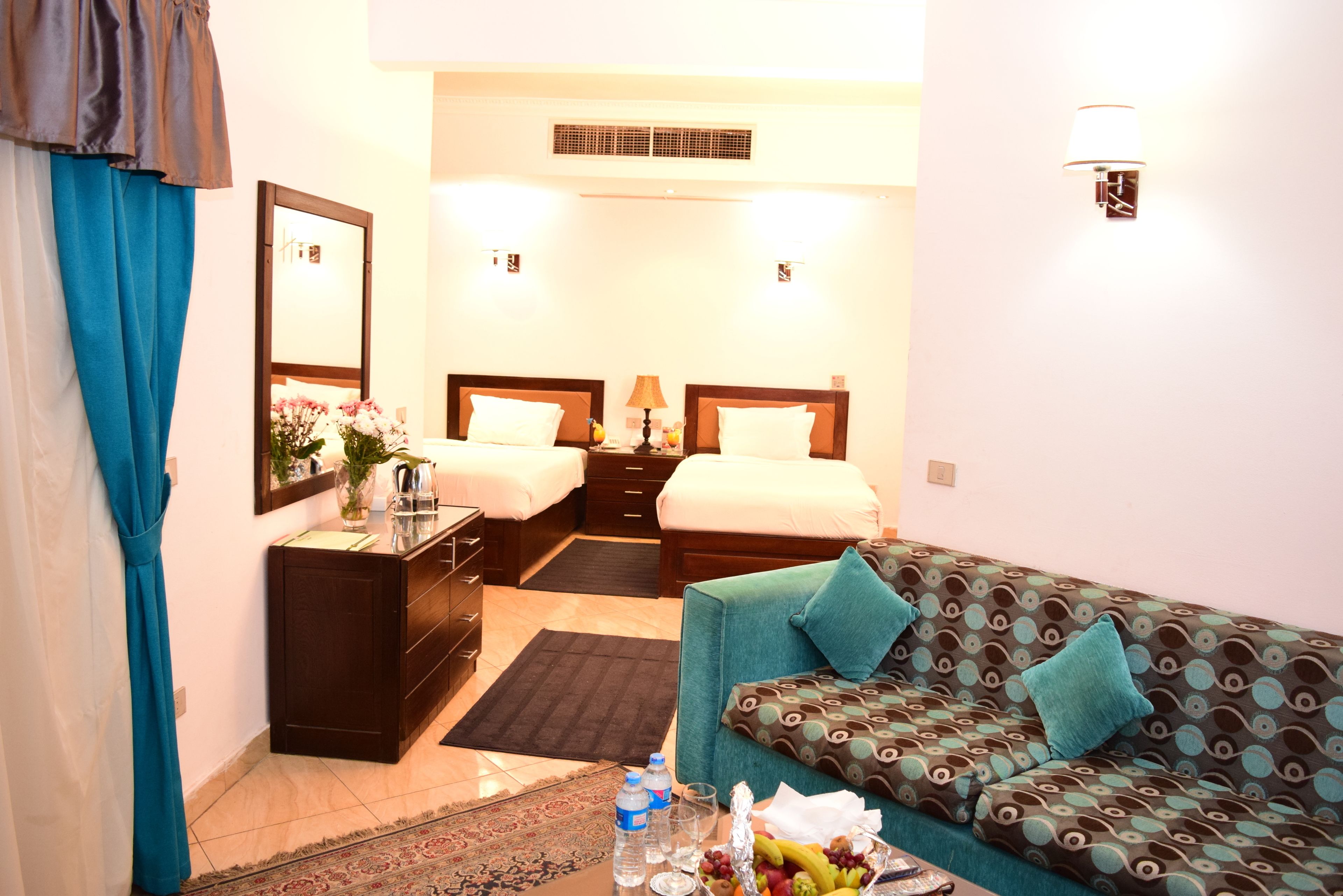Quarto de hotel com duas camas, um sofá, uma cômoda e um espelho.