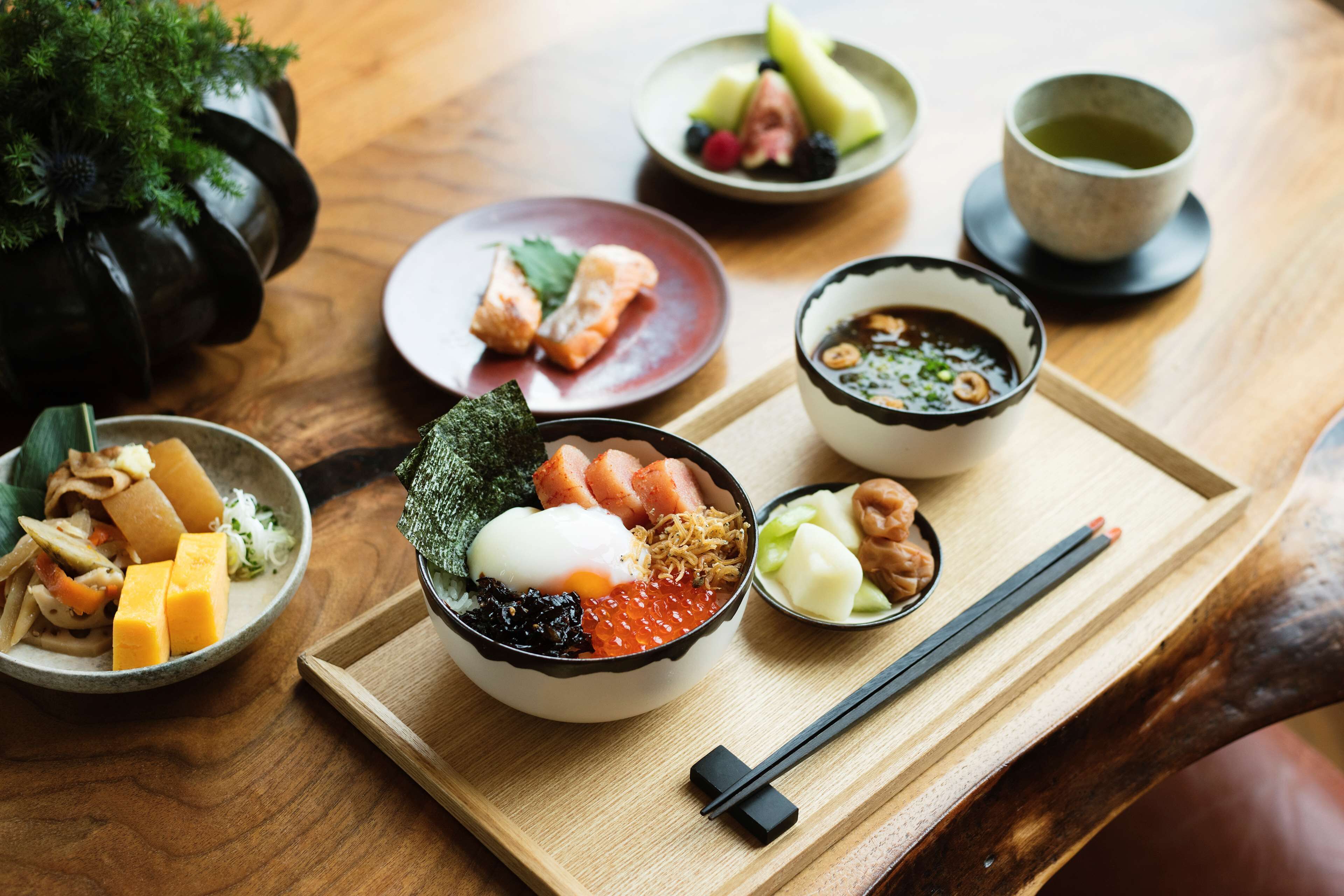 Uma mesa de madeira com diversos pratos, incluindo uma tigela de ramen, um prato de sashimi e uma sopa.