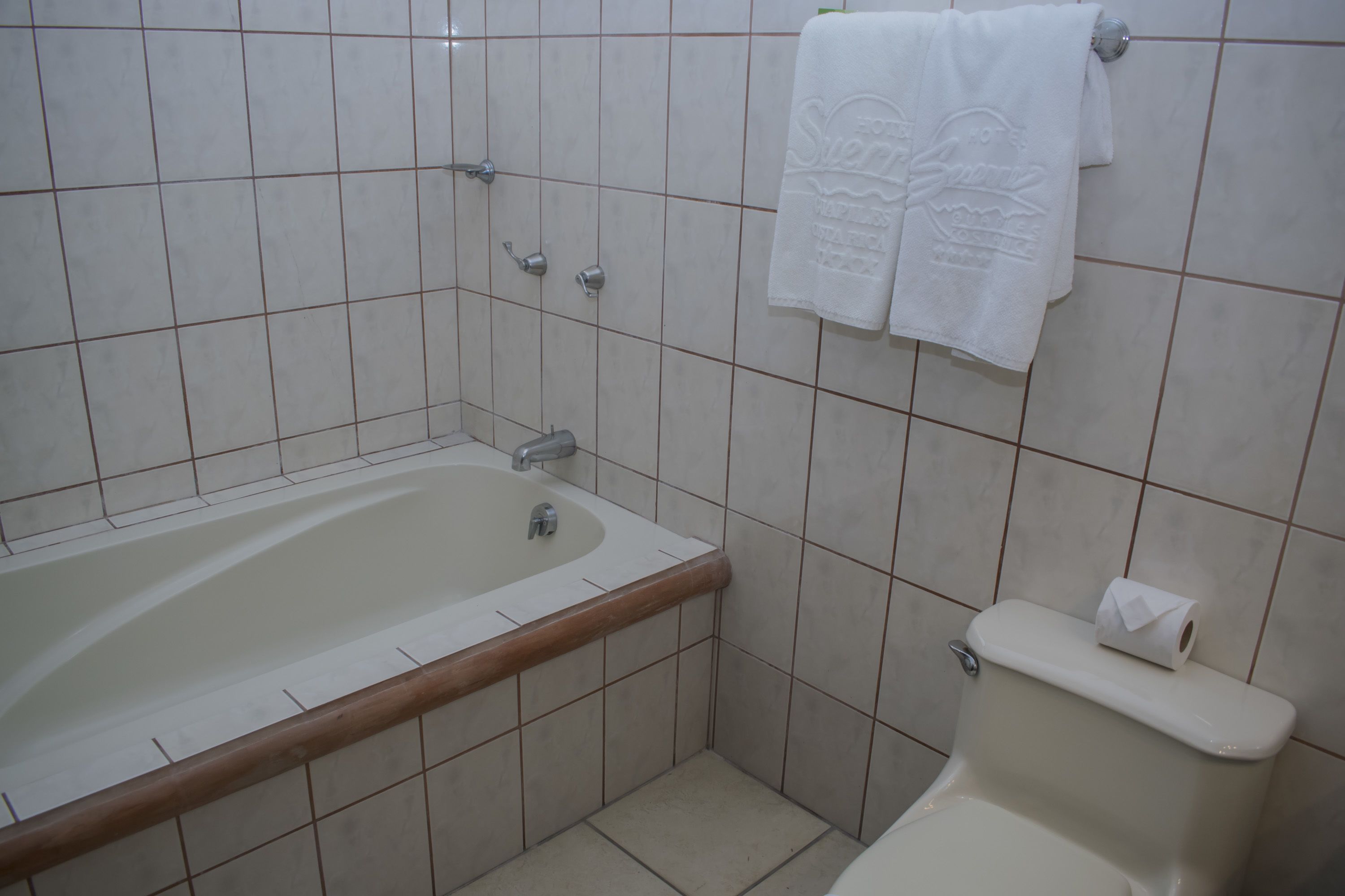 Um banheiro com banheira, vaso sanitário e duas toalhas penduradas na parede.