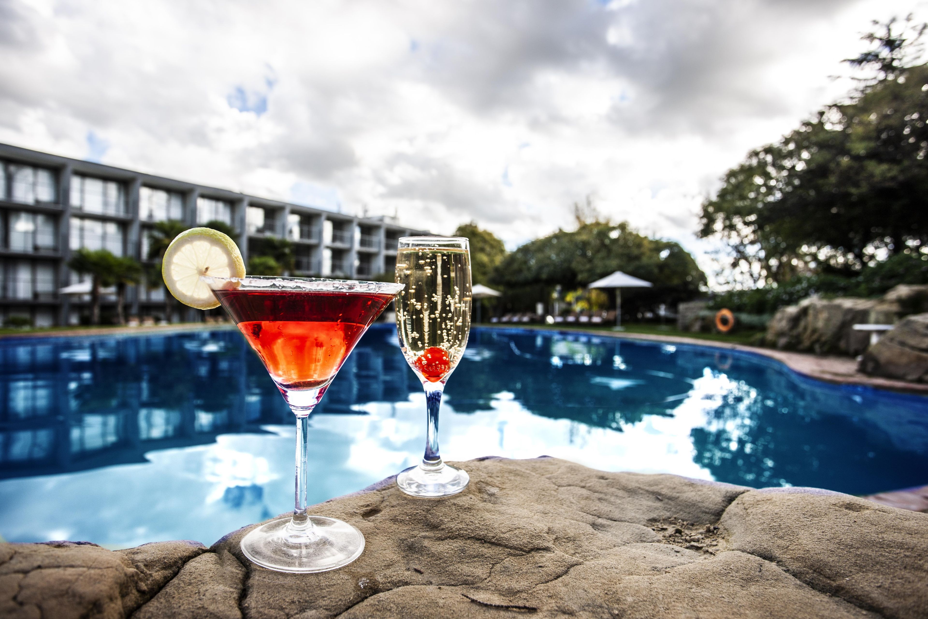 Dois cocktails sobre uma rocha, perto de uma piscina, com um edifício ao fundo.