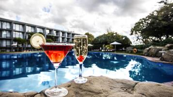 Dois cocktails sobre uma rocha, perto de uma piscina, com um edifício ao fundo.