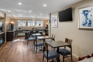 Uma sala de jantar moderna com mesas e cadeiras, uma cozinha ao fundo e obras de arte nas paredes.