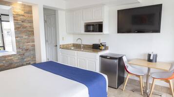Quarto de hotel com cama, cozinha compacta, televisão e secretária com cadeiras.