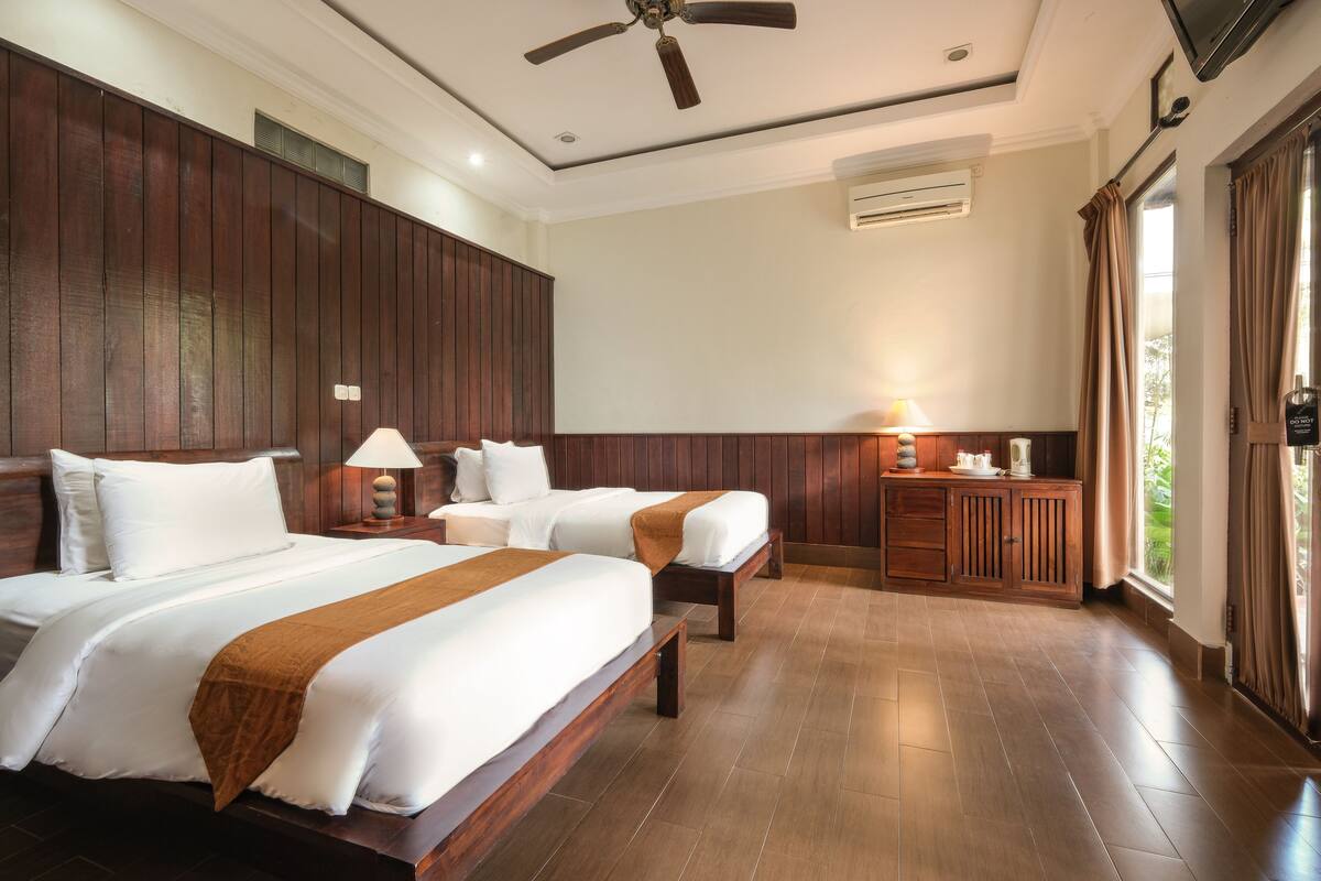 Quarto de hotel com uma cama grande, duas mesas de cabeceira, um armário de madeira e um ventilador de teto.