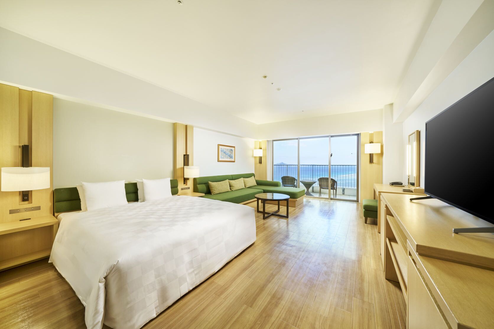 Quarto de hotel com uma cama grande, um sofá, uma TV e uma varanda vista para o mar.