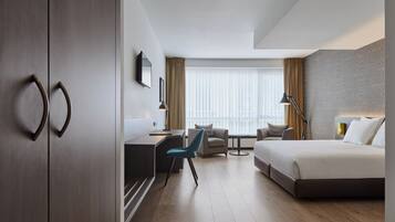 Quarto de hotel com cama, escrivaninha, cadeira, mesinha e luminária.