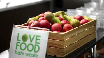 Uma caixa de madeira cheia de maçãs e peras vermelhas e verdes, com uma placa que diz 'LOVE FOOD hate waste'.