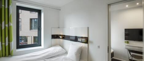Quarto de hotel moderno com cama, escrivaninha, televisão e janela com cortinas.