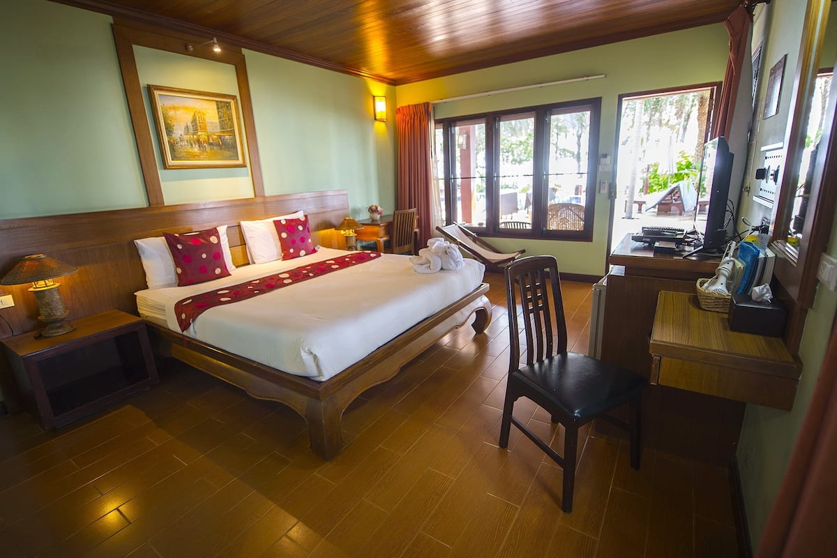 Quarto de hotel com cama, escrivaninha, cadeira e janelas amplas.