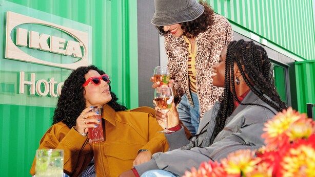 Um grupo de pessoas sentadas à mesa com comida e bebidas em frente a um edifício verde onde se lê 'Grillen' e 'IKEA'.