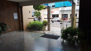 Entrada de hotel com porta de vidro, chão xadrez e rua visível.