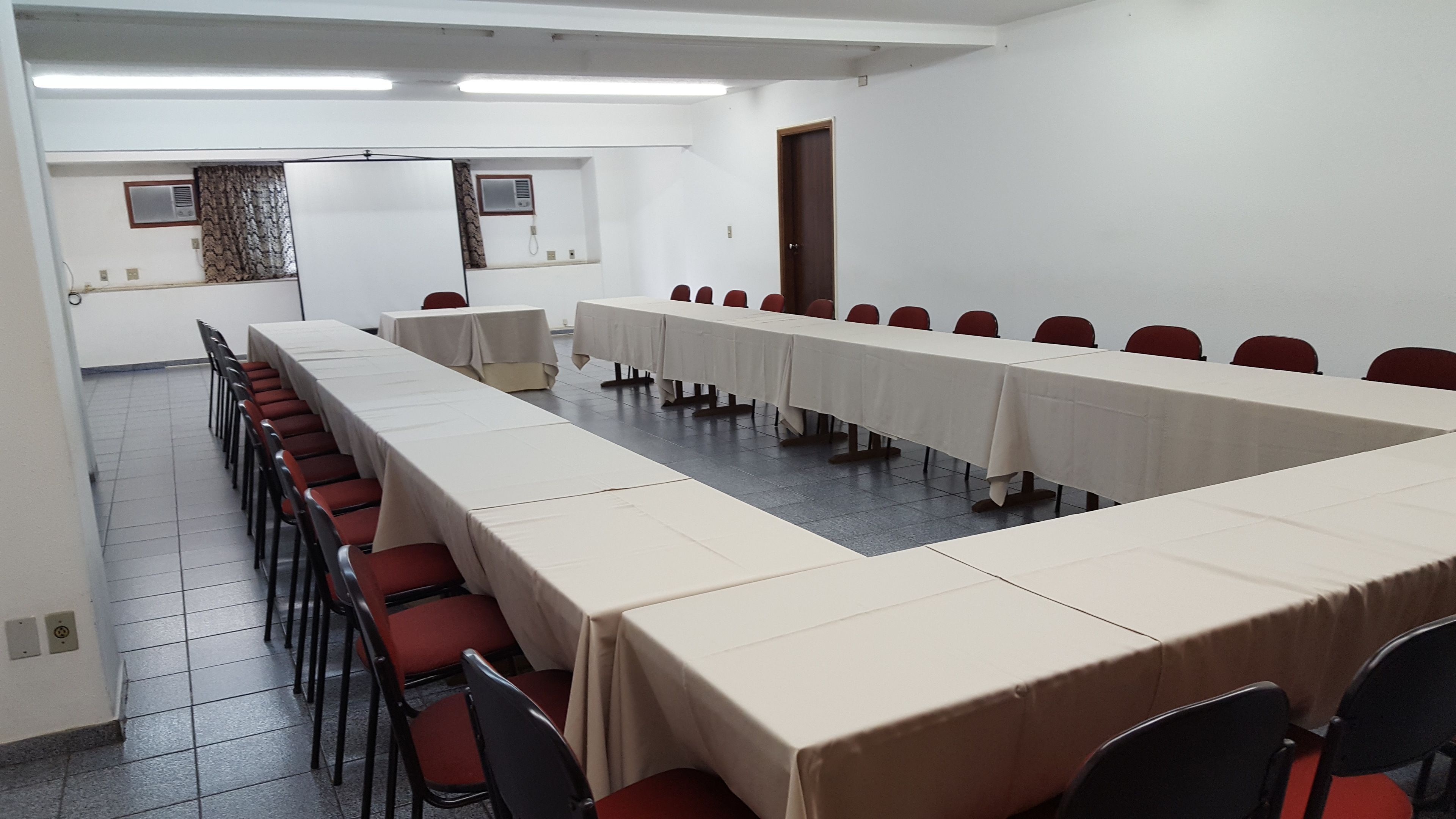 Uma sala de conferências com uma mesa comprida e cadeiras, paredes brancas e chão de azulejos.
