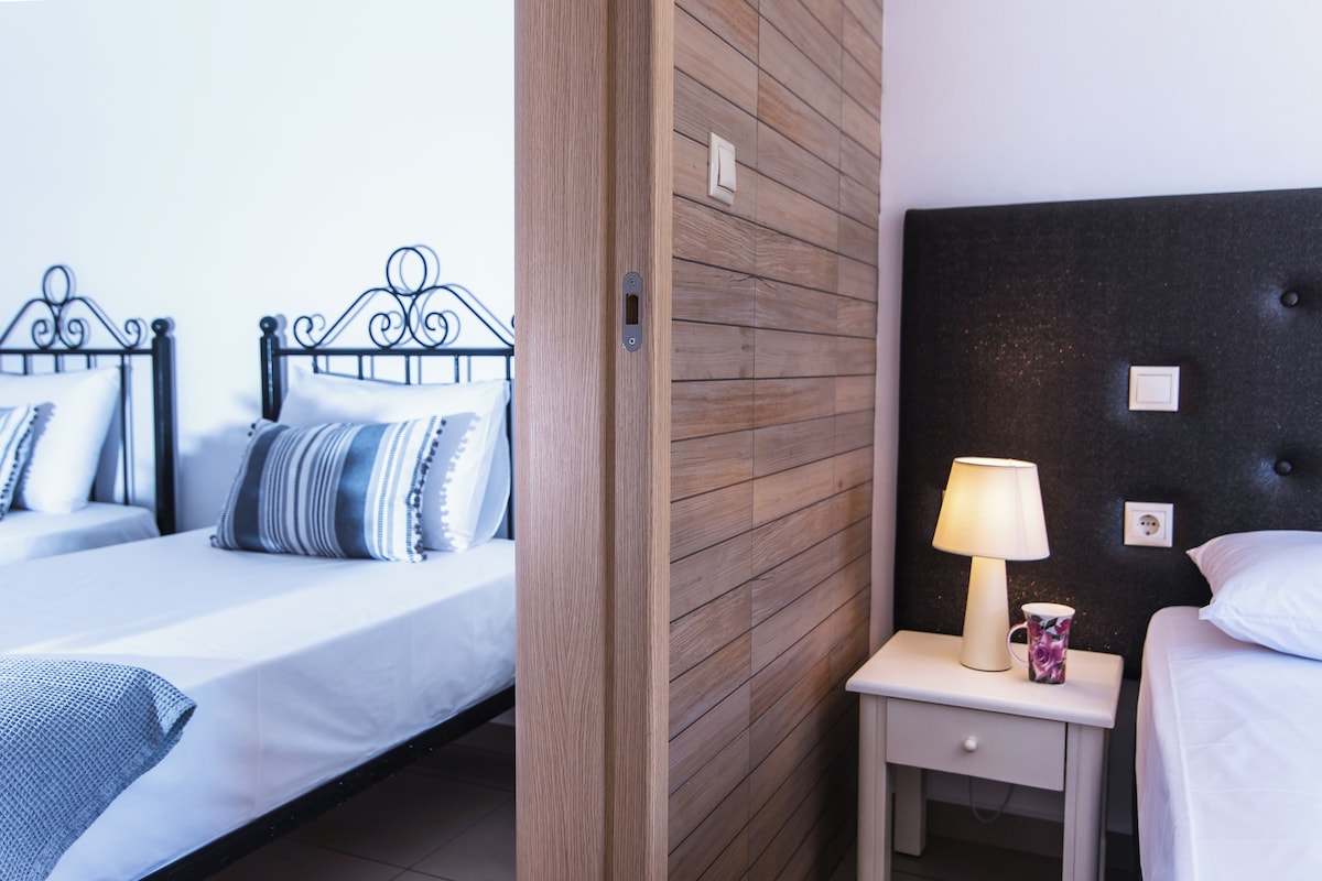 Quarto de hotel com duas camas, parede de painel de madeira, mesa de cabeceira com abajur e uma caneca decorativa.