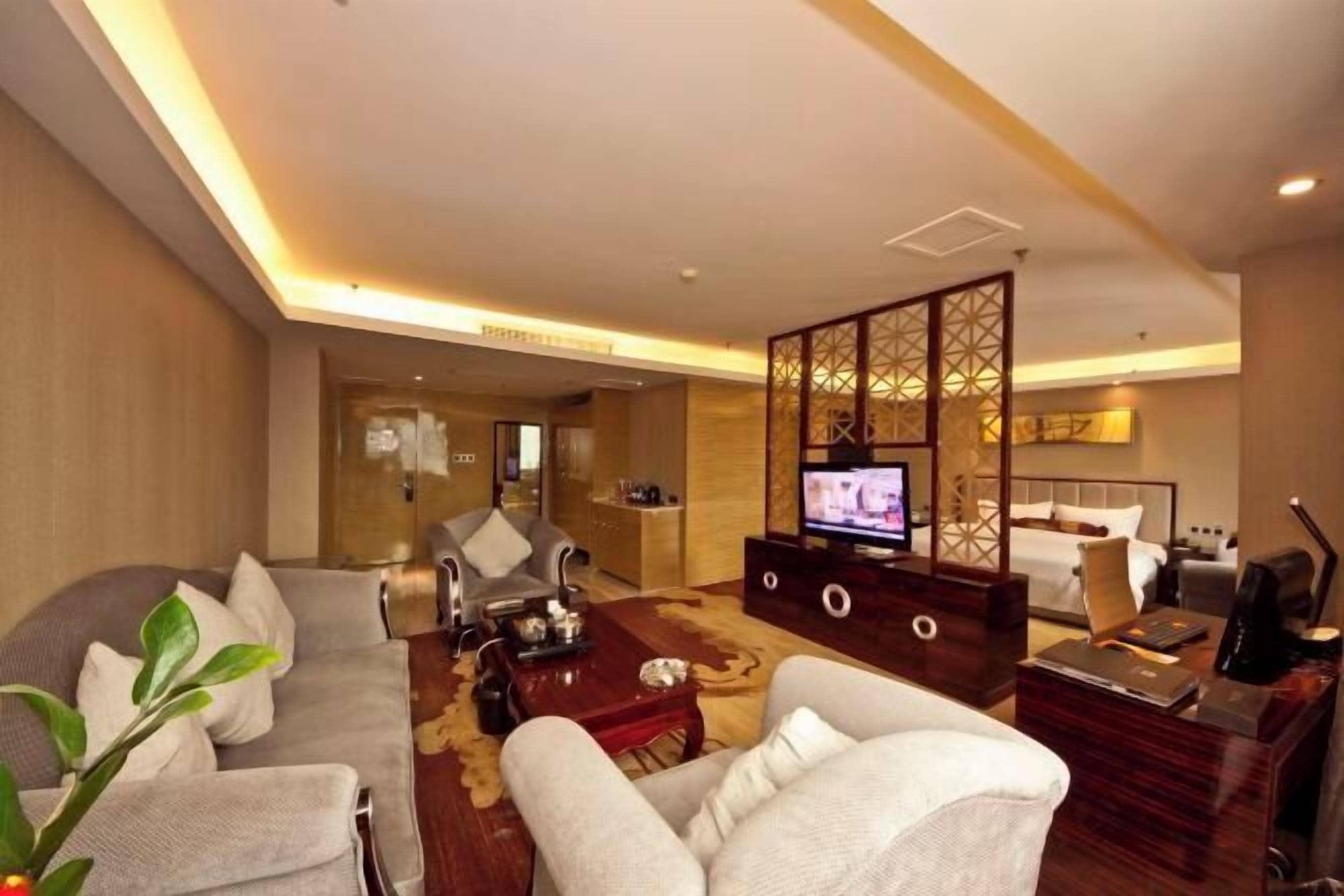 Quarto de hotel moderno com sofá, poltronas, televisão, escrivaninha e cama.