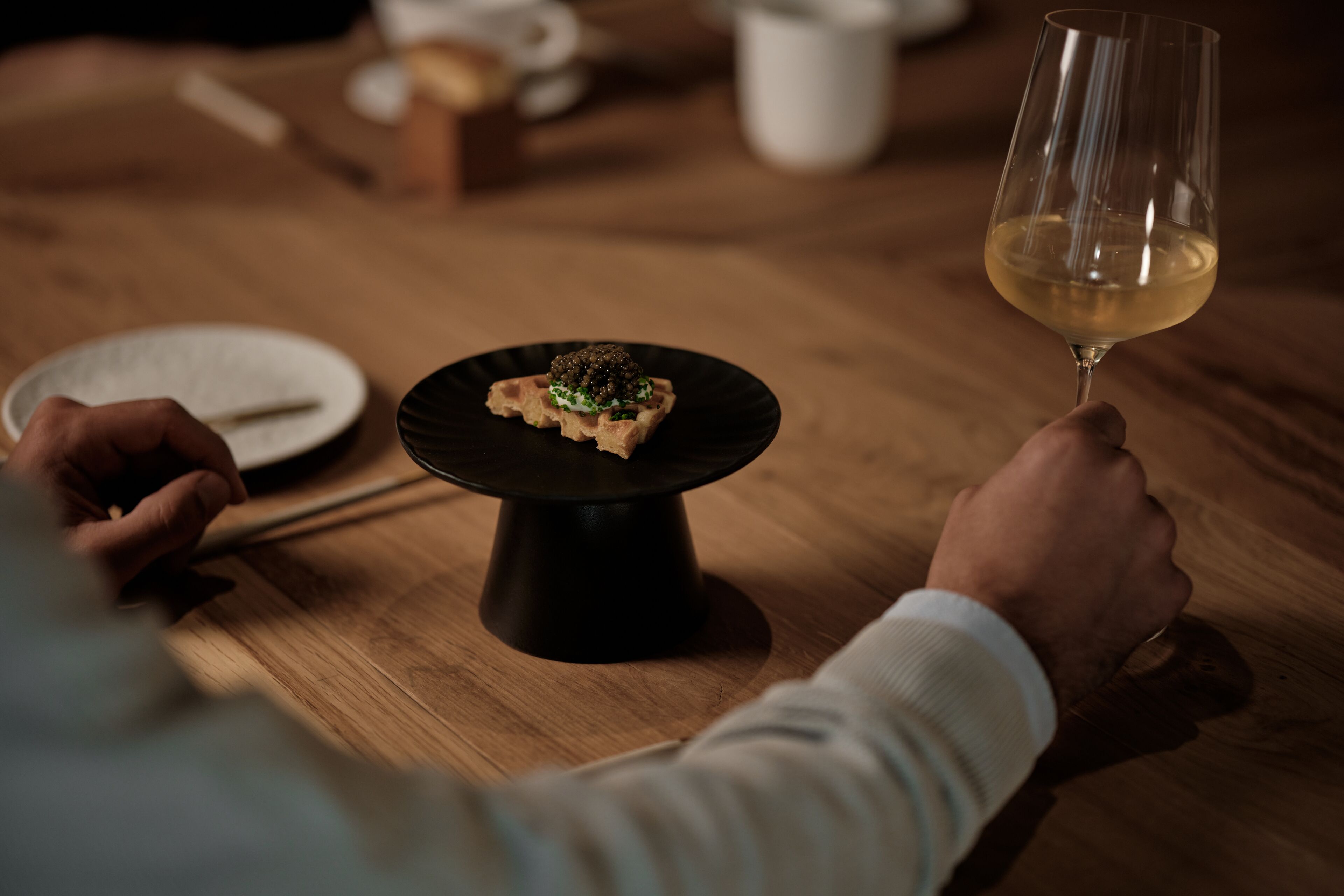 Uma pessoa segurando uma taça de vinho com uma sobremesa em um prato preto.