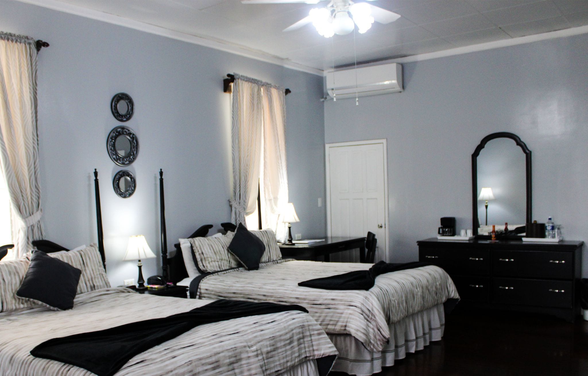 Quarto de hotel com duas camas, uma escrivaninha, uma cadeira, uma cômoda, um espelho e um ar condicionado.