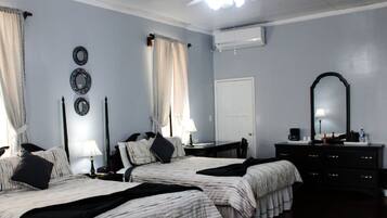 Quarto de hotel com duas camas, uma escrivaninha, uma cadeira, uma cômoda, um espelho e um ar condicionado.