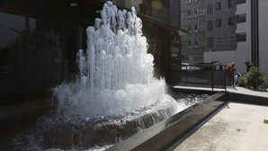Uma fonte de água em ambiente urbano, com edifícios modernos ao fundo.