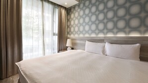 Quarto de hotel com uma cama grande, mesa de cabeceira com abajur e parede estampada.