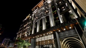 Hotel moderno com fachada de vidro, área de estar externa e terraço no telhado.