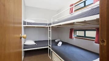 Quarto com beliche, porta de madeira, escada e janela com cortinas.