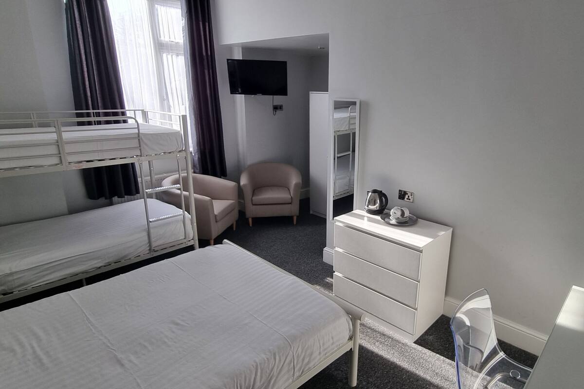 Quarto de hotel com beliches, uma cadeira, cômoda, televisão de tela plana e uma mesa pequena.