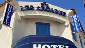 Um hotel chamado "LES ARCADES" com um toldo azul bem visível e uma porta azul.
