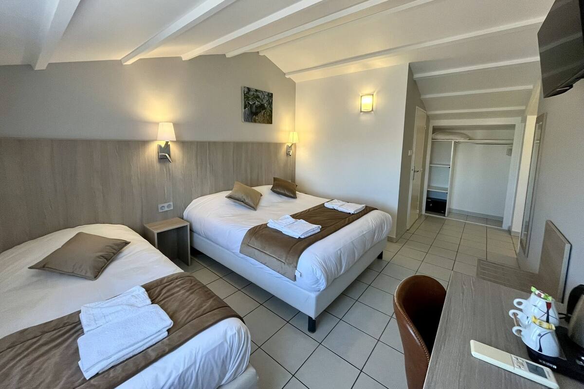Quarto de hotel com duas camas, uma escrivaninha e uma cadeira. Há luminárias fixadas na parede e um quadro na parede.