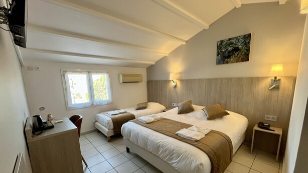 Quarto de hotel com duas camas, uma escrivaninha, uma cadeira, uma janela e um quadro na parede.
